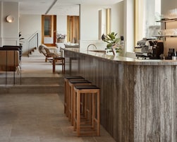 Uma cozinha moderna com uma ilha central, banquetas, uma máquina de café e vista para a área de jantar.