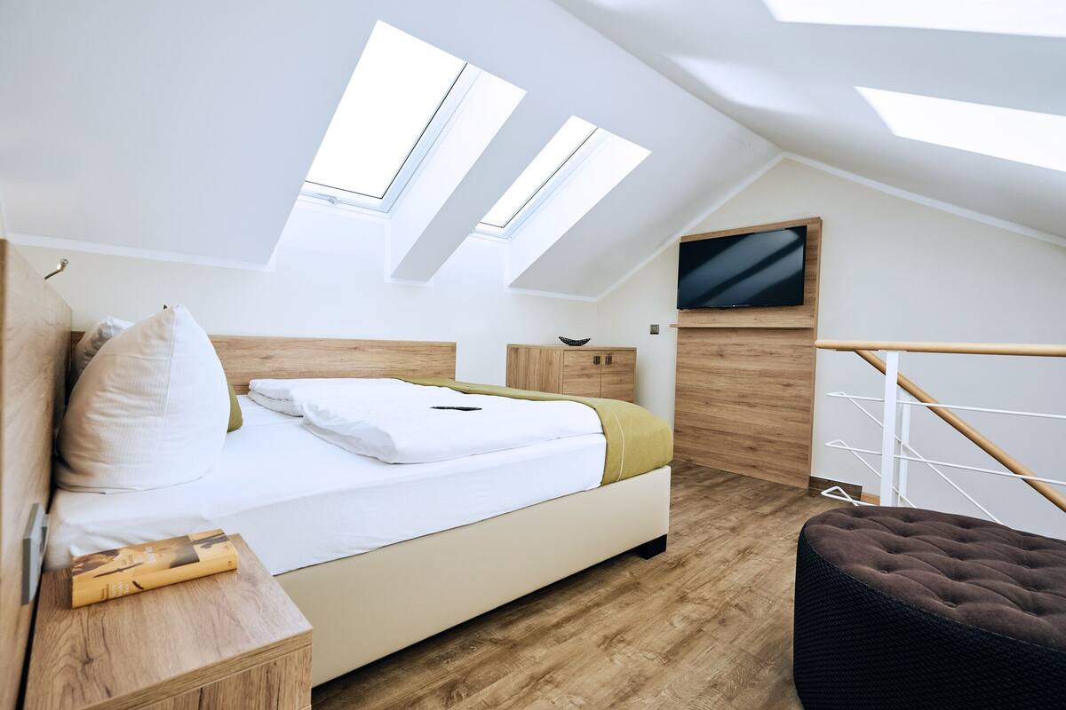 Um quarto moderno com claraboia, uma cama, uma mesa de cabeceira de madeira, uma TV fixada na parede e uma escada.