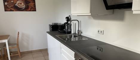 Uma cozinha moderna com bancada de aço inoxidável, forno embutido, máquina de café e uma TV de tela plana fixada acima da bancada.