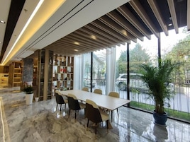 Um lobby de hotel moderno com piso de mármore, um balcão de recepção alongado e uma área de estar com mesa e cadeiras.