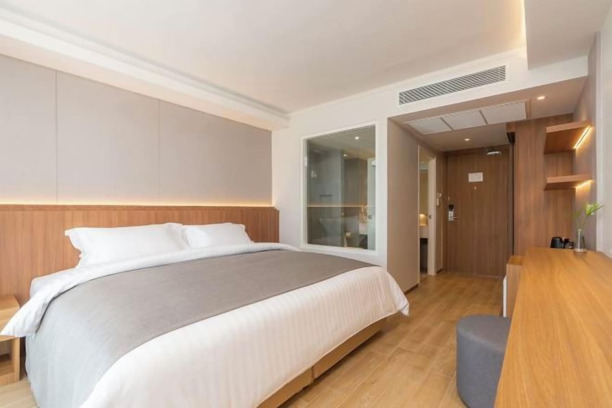 Quarto de hotel moderno com uma cama grande, uma escrivaninha de madeira e um painel de parede de vidro.