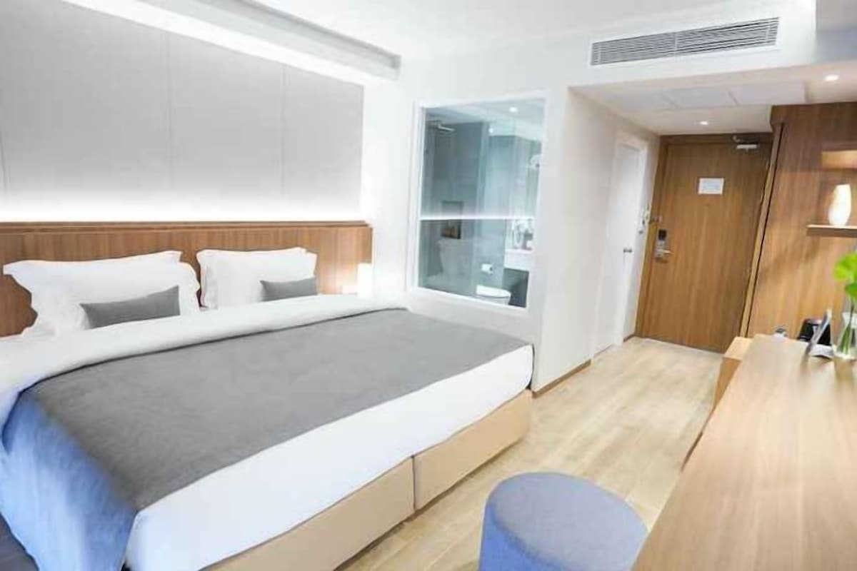 Quarto de hotel moderno com uma cama grande, cabeceira de madeira, uma janela e uma escrivaninha de madeira.