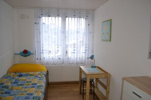 Quarto pequeno e arrumado com uma cama, uma escrivaninha e uma cadeira.
