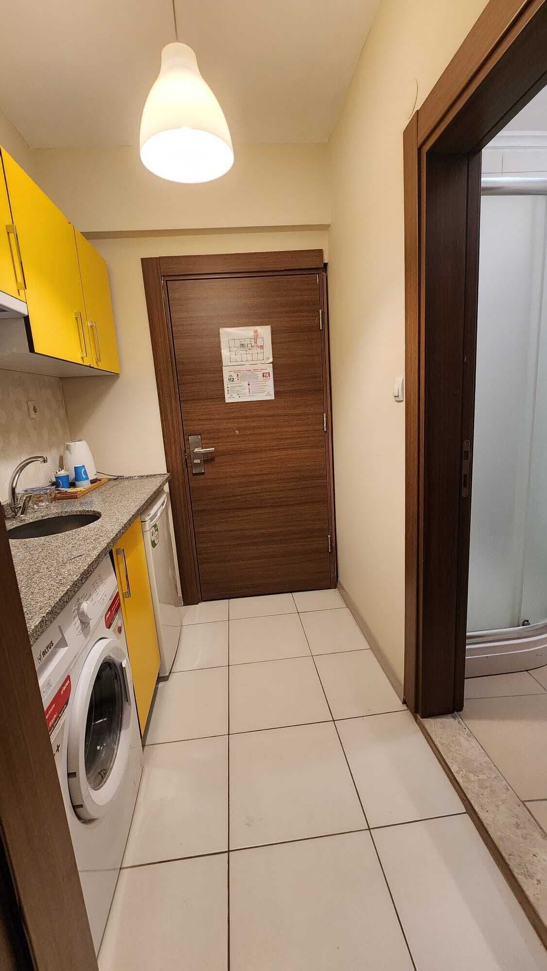 Cozinha compacta com máquina de lavar, pia e porta de madeira com aviso.