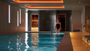 Uma piscina com uma pessoa caminhando na água, uma sauna e uma estátua.