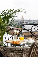 Uma mesa de vime com itens de café da manhã, um copo de suco de laranja e uma xícara de café, com vista para a cidade.