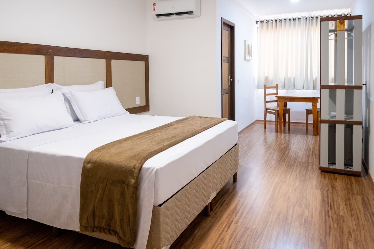 Quarto de hotel com cama, piso de madeira, uma pequena mesa com cadeiras e um guarda-roupa.