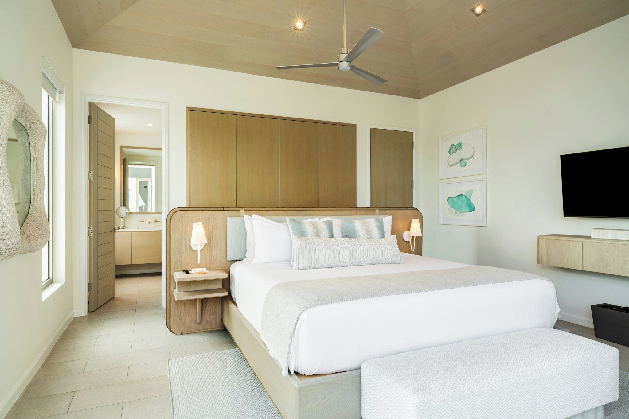 Quarto moderno com uma cama grande, cabeceira de madeira, mesas de cabeceira, um ventilador de teto e uma TV sobre um console de madeira.