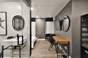 Quarto de hotel moderno com uma cama, uma escrivaninha, uma cadeira, um espelho redondo e um guarda-roupa.