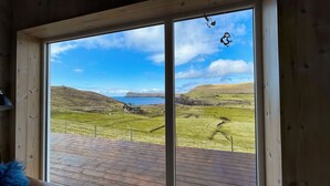 Quarto com uma janela ampla que oferece vista para uma paisagem costeira, incluindo colinas e um corpo de água.