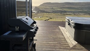 Um terraço com churrasqueira e banheira de hidromassagem, com vista para uma paisagem costeira com campos e falésias.