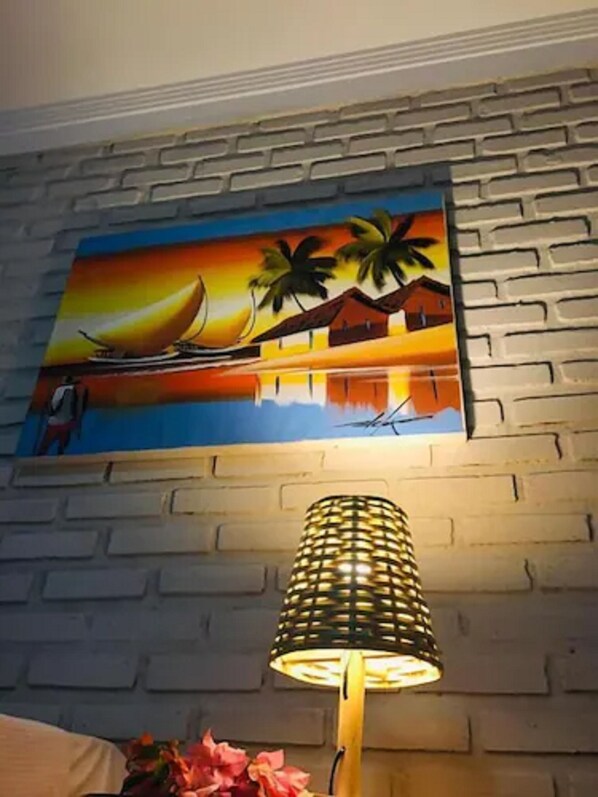 Uma parede com pintura de pôr do sol, um abajur e um vaso com flores.