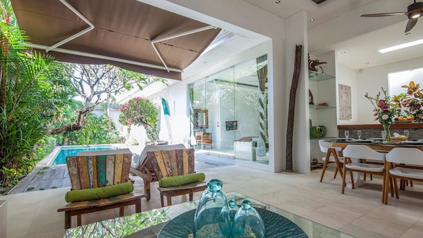 Uma sala de estar moderna com uma mesa de vidro, cadeiras de madeira e vista para uma piscina.