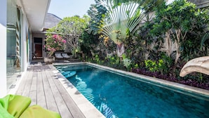 Piscina com deck de madeira, rodeada por vegetação tropical exuberante e um edifício de vidro.