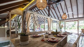 Uma área de jantar de madeira com uma mesa comprida, diversos pratos e um lustre pendurado.