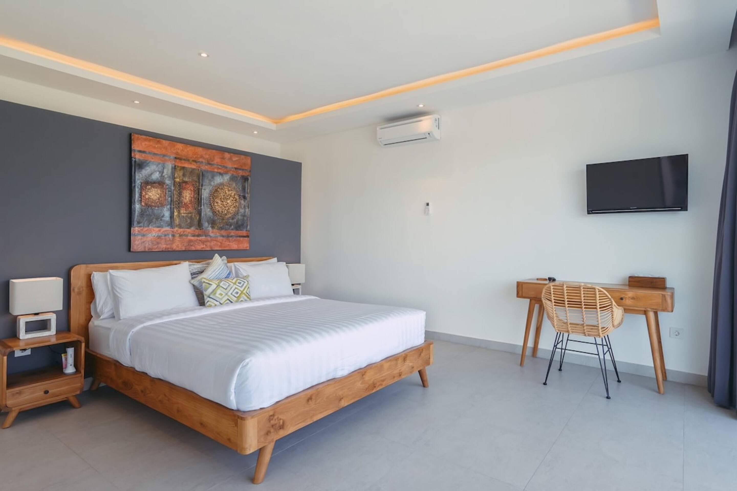 Quarto moderno com cama de madeira, escrivaninha e cadeira, televisão de tela plana e um grande quadro abstrato na parede.
