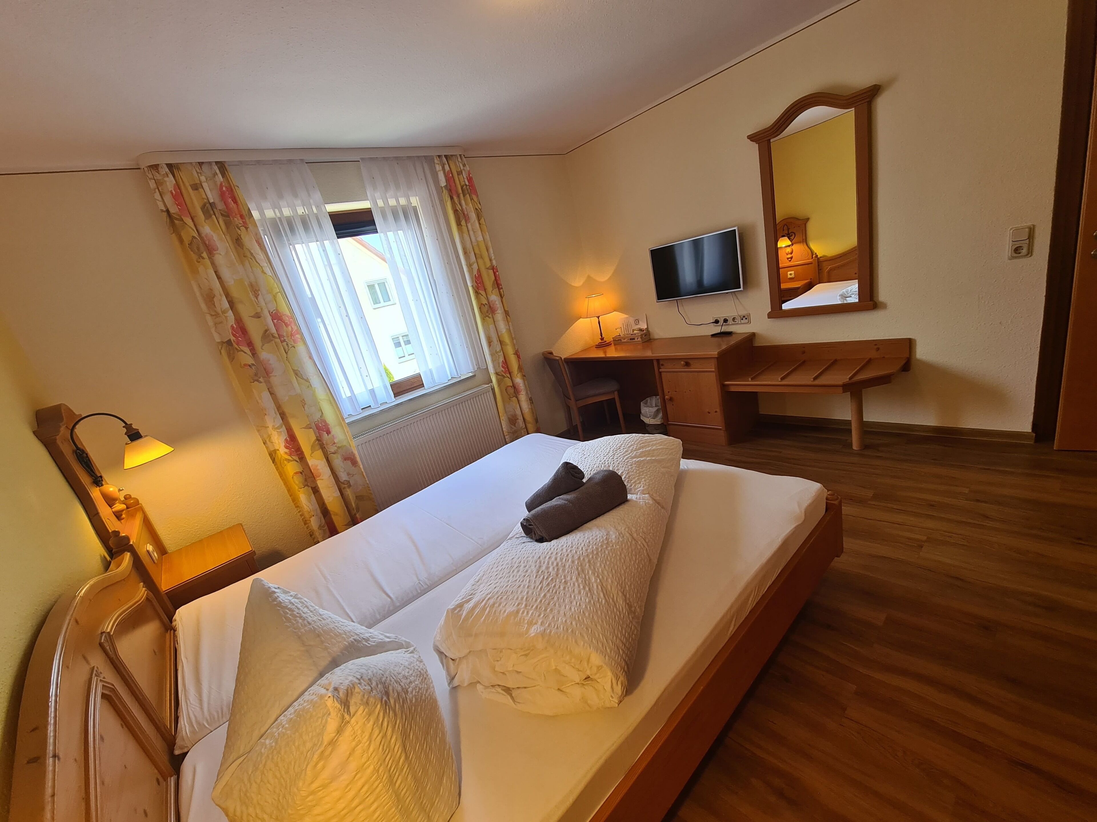 Quarto de hotel com cama, escrivaninha, televisão e espelho.