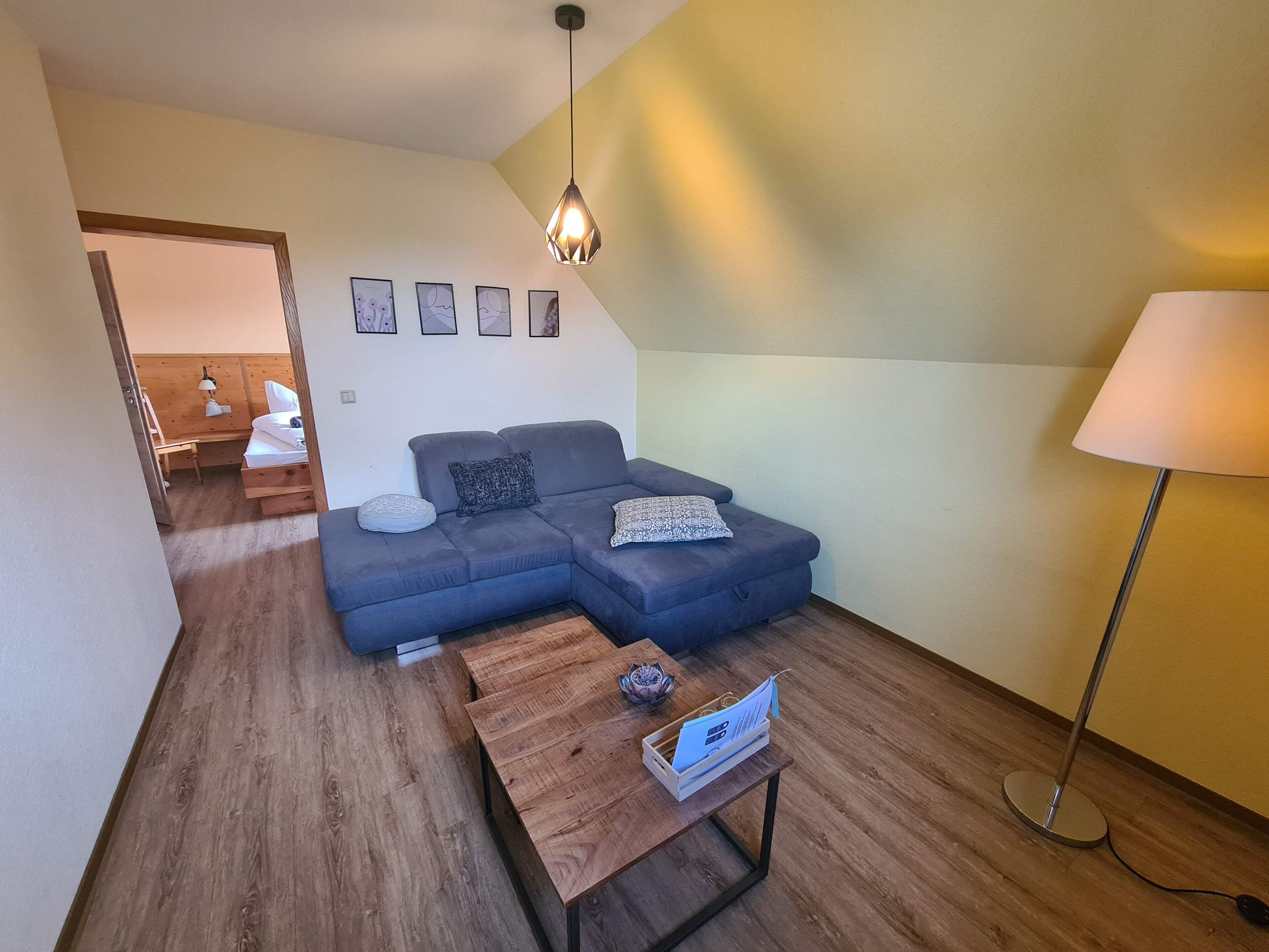 Uma sala de estar moderna com um sofá seccional, uma mesa de centro de madeira, um abajur e uma luminária fixada na parede.