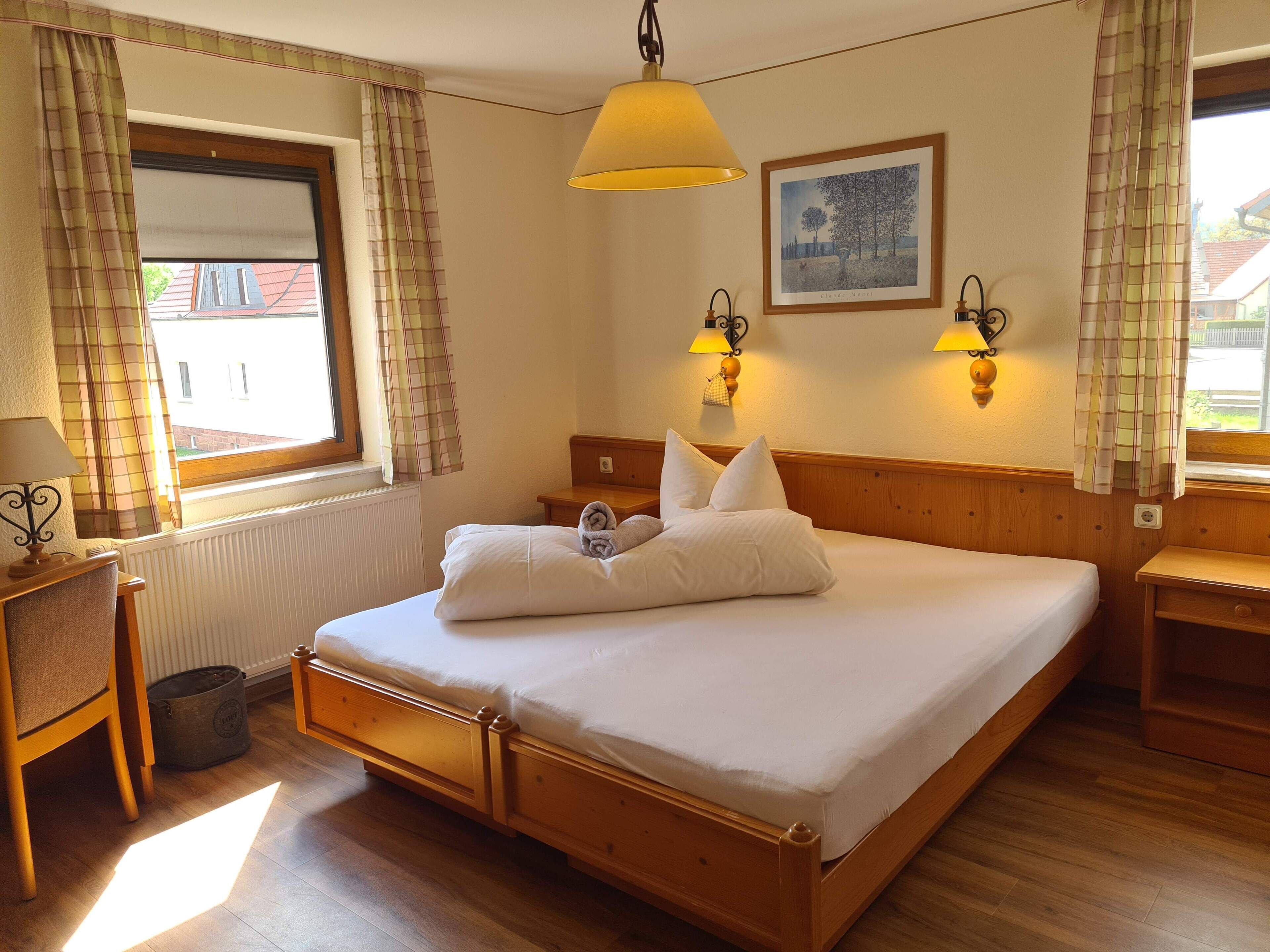 Quarto com cama de madeira, duas luminárias de cabeceira, janela com cortinas, radiador e quadro na parede.