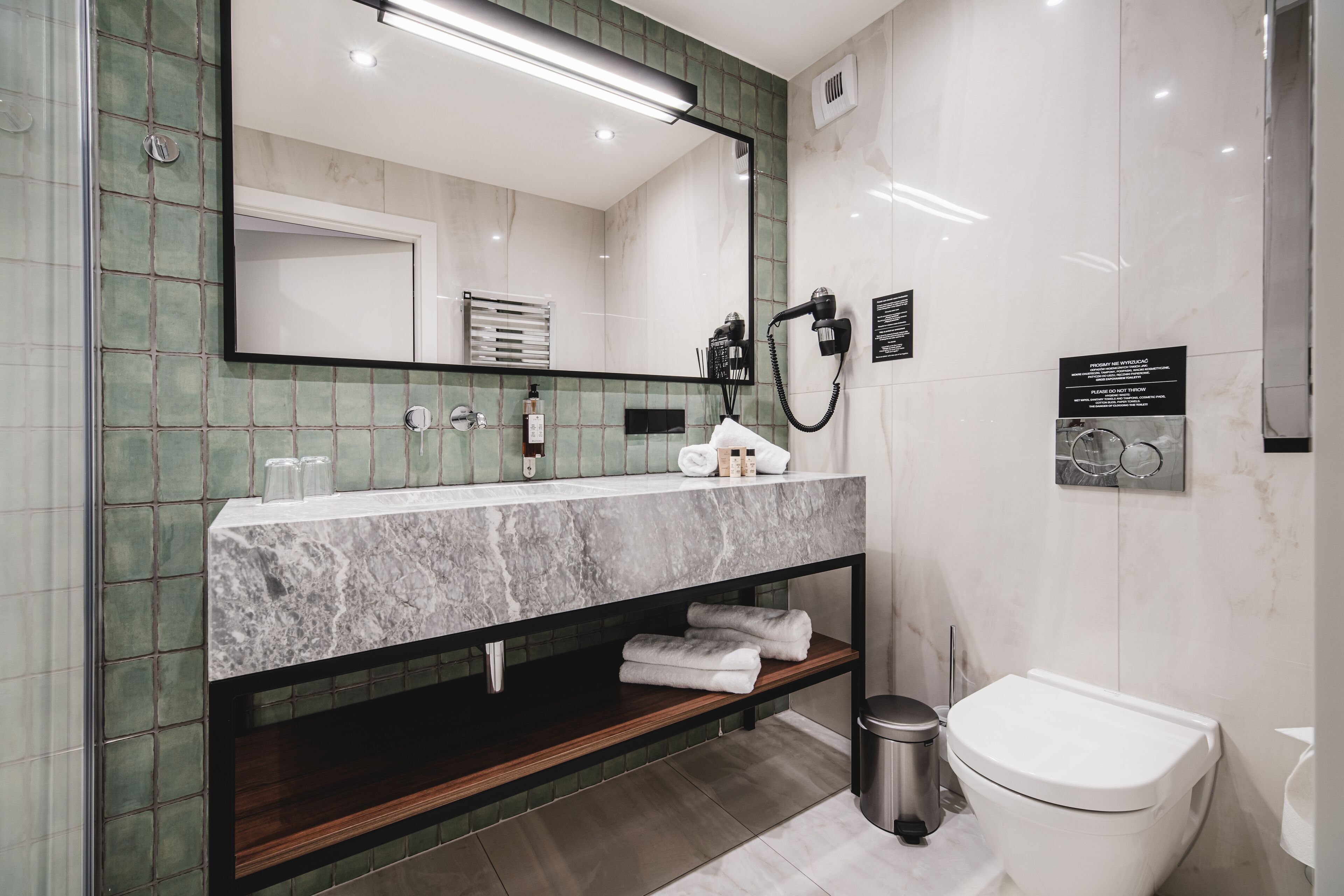 Um banheiro moderno com toucador de mármore, um espelho grande, um secador de cabelo e vaso sanitário.
