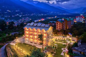 Um hotel com vários andares, área externa bem iluminada e vista para montanhas ao redor.