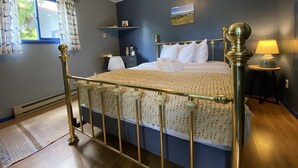 Quarto com cama, mesa de cabeceira, abajur e janela com cortinas.