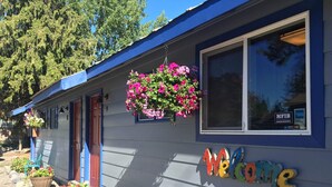 Um edifício com uma placa de 'Welcome', uma porta e cestos com flores penduradas.