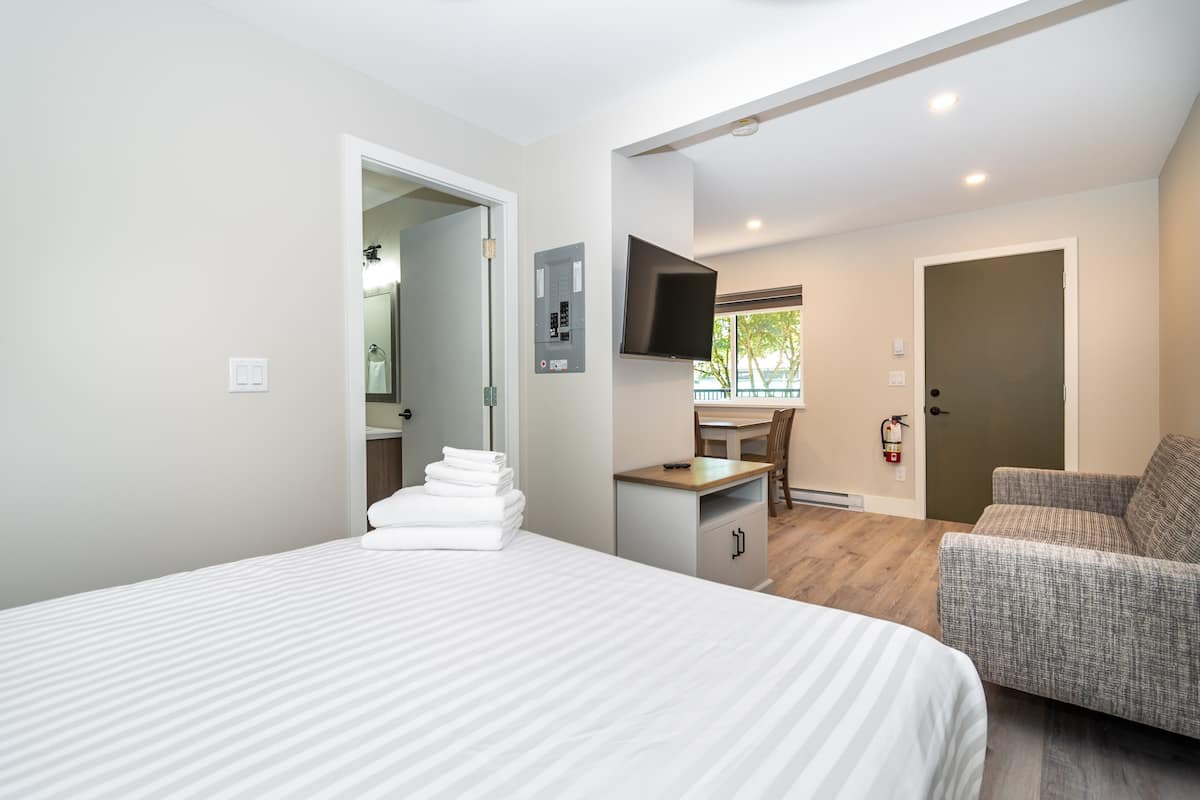 Quarto de hotel com cama, escrivaninha, cadeira e televisão.