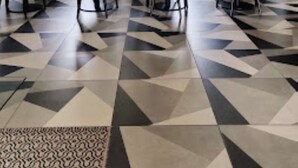 Uma sala de jantar com mesas e cadeiras, piso estampado e uma janela com vista para vegetação.