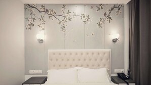 Quarto de hotel com cama, mesas de cabeceira, telefone fixado na parede e um mural decorativo com flores.