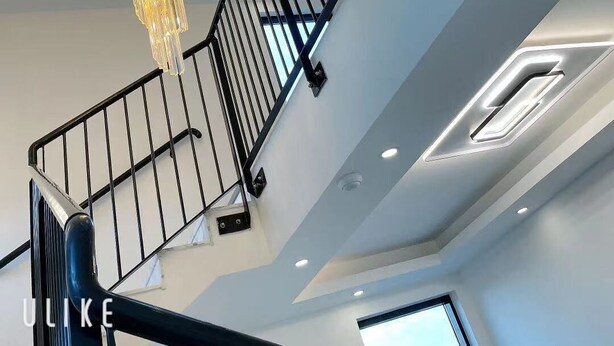 Um interior moderno com um lustre imponente, uma escadaria de metal preto e um claraboia.