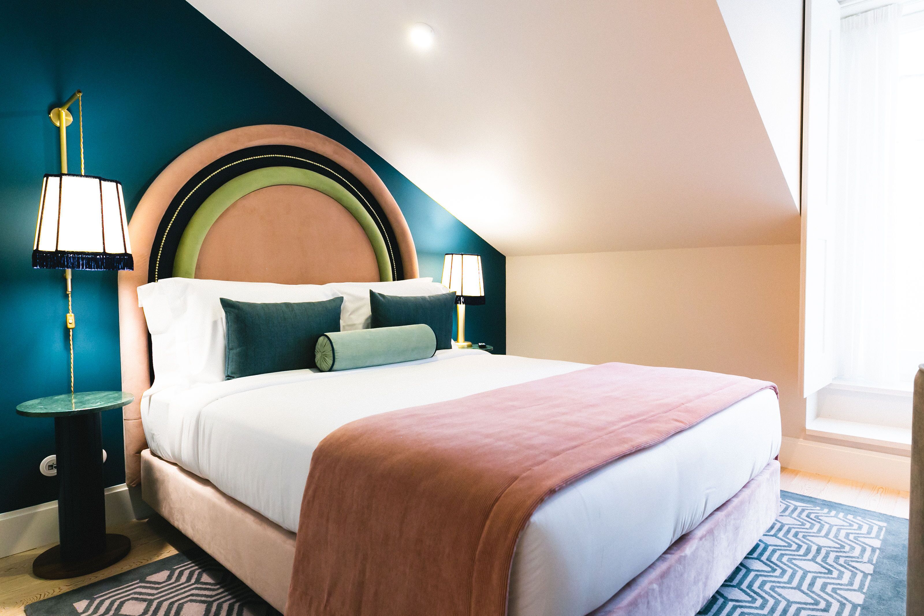Quarto moderno com cama grande, duas luminárias de cabeceira, cabeceira redonda e vista para o exterior através de uma janela.
