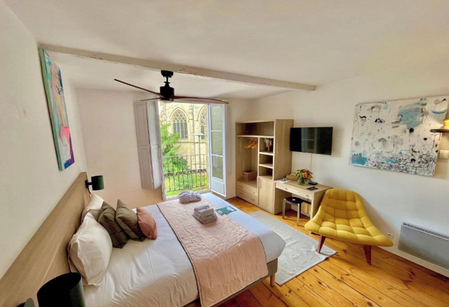 Quarto com cama, escrivaninha, cadeira, televisão e varanda com vista para um edifício.