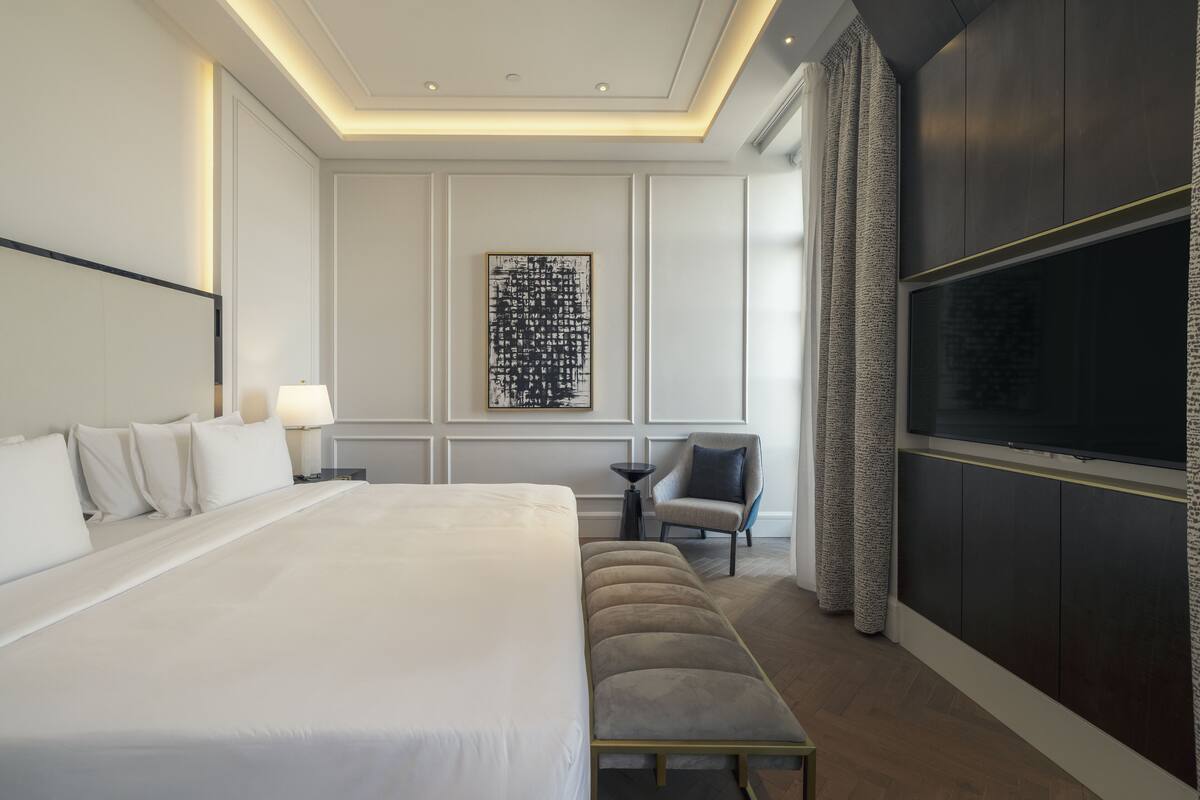 Quarto de hotel moderno com cama grande, televisão de tela plana, área de estar e um detalhe decorativo na parede.