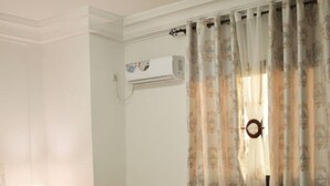 Quarto com cama, luminária de cabeceira, ar condicionado e cortinas estampadas.