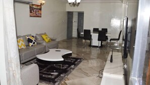 Uma sala de estar moderna com um sofá cinzento, uma mesa de centro redonda e um espaço de refeições com mesa branca e cadeiras pretas.