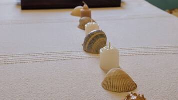 Uma mesa com conchas decorativas e velas, uma janela com vista para o verde, e uma parede verde-água com prateleiras.