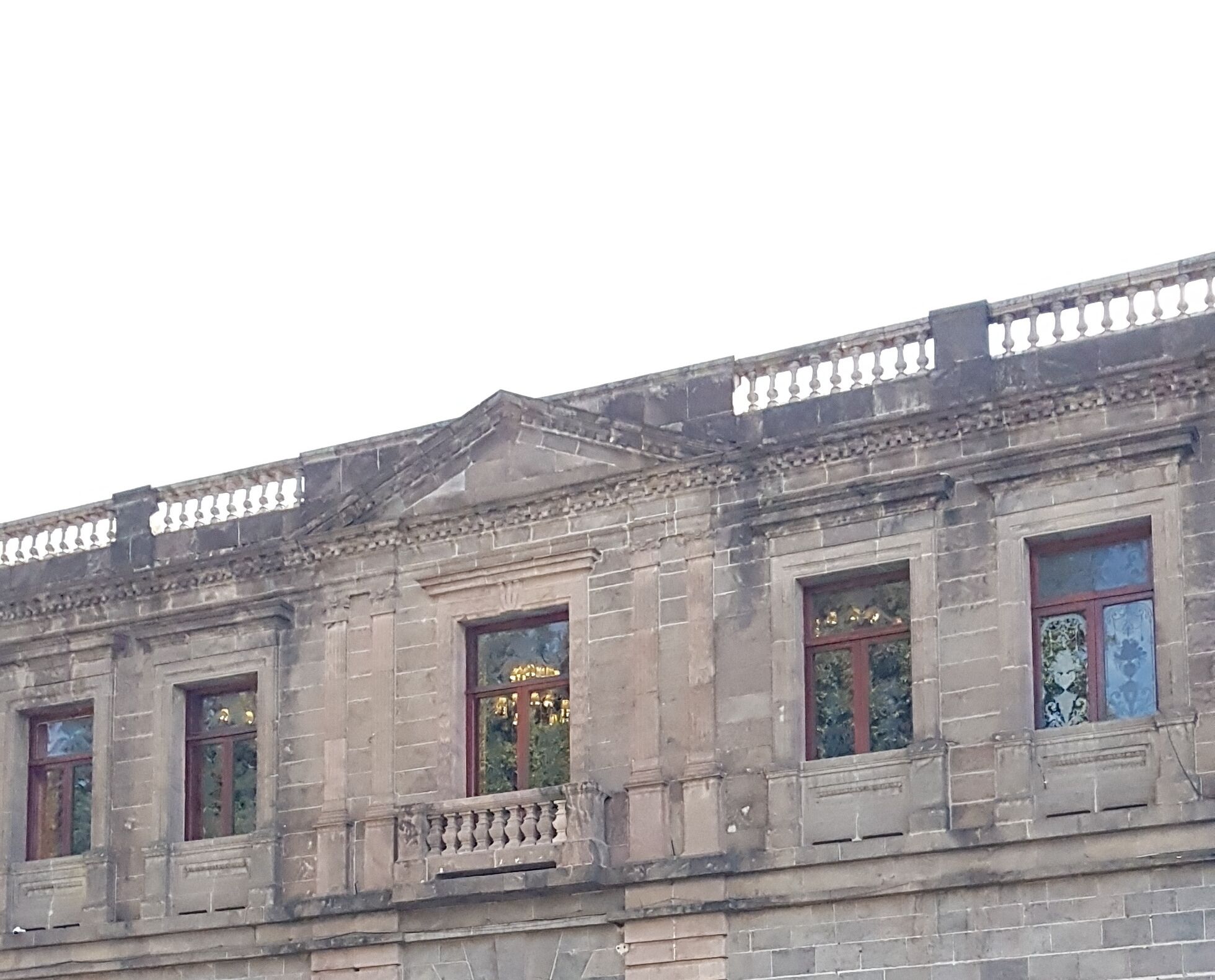 Um edifício histórico com fachada de pedra, várias janelas com molduras ornamentadas e uma varanda com balaústres.