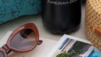 Um folheto com vista para a piscina, uma garrafa de água preta com a inscrição 'Hyatt Centric Jumeirah Dubai' e um par de óculos de sol.