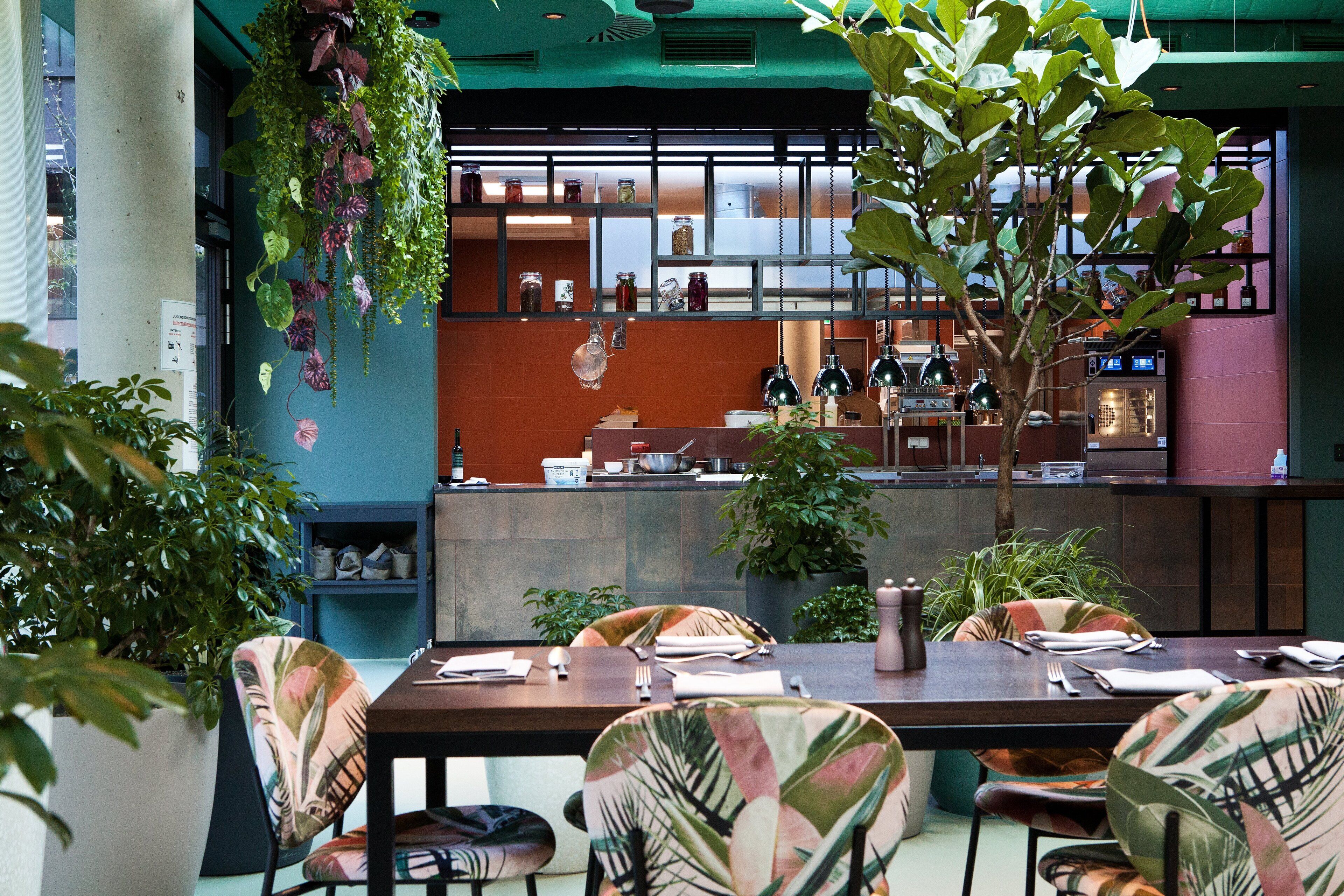 Um restaurante com uma mesa comprida, cadeiras, plantas penduradas e um balcão com prateleiras.