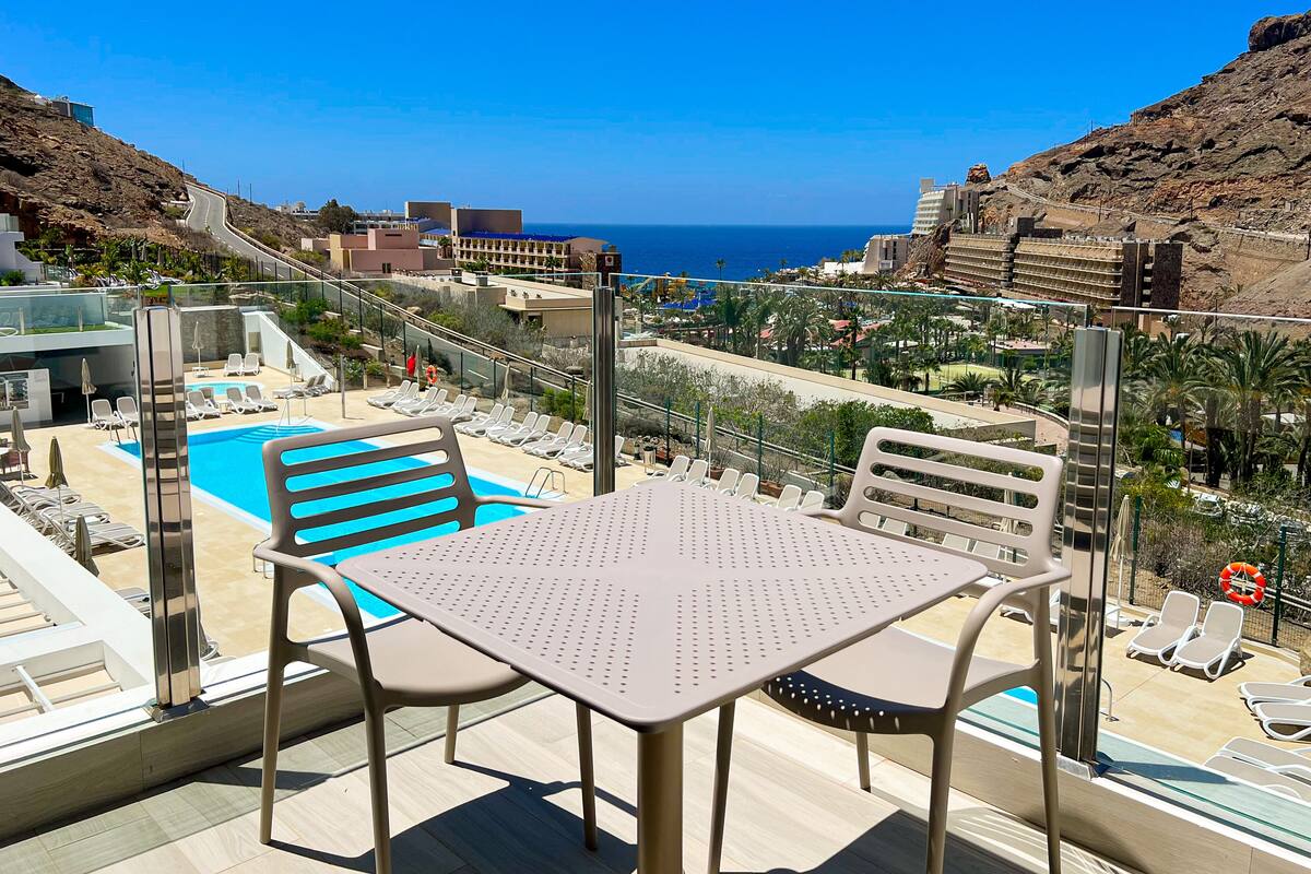 Varanda com mesa e cadeiras, vista para uma piscina e para o litoral.