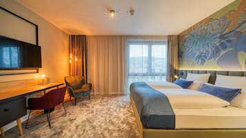 Quarto de hotel com uma cama grande, uma escrivaninha, uma cadeira e uma televisão.