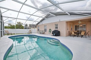 Piscina interna com teto de vidro, cercada por espreguiçadeiras e área de churrasco.