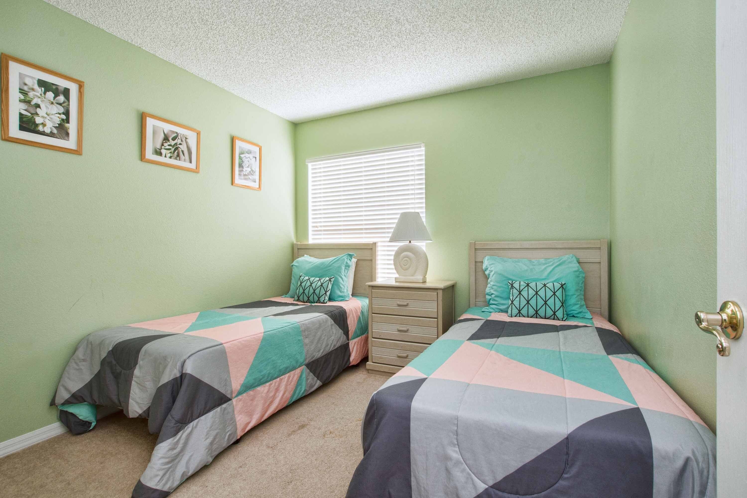 Quarto com duas camas, cômoda, janela com persianas e quadros na parede.