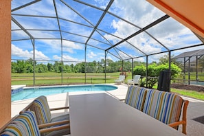 Área externa coberta com piscina, assentos e vista para uma paisagem verde.