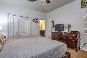 Quarto com uma cama grande, cômoda, televisão e porta que dá para outro ambiente.