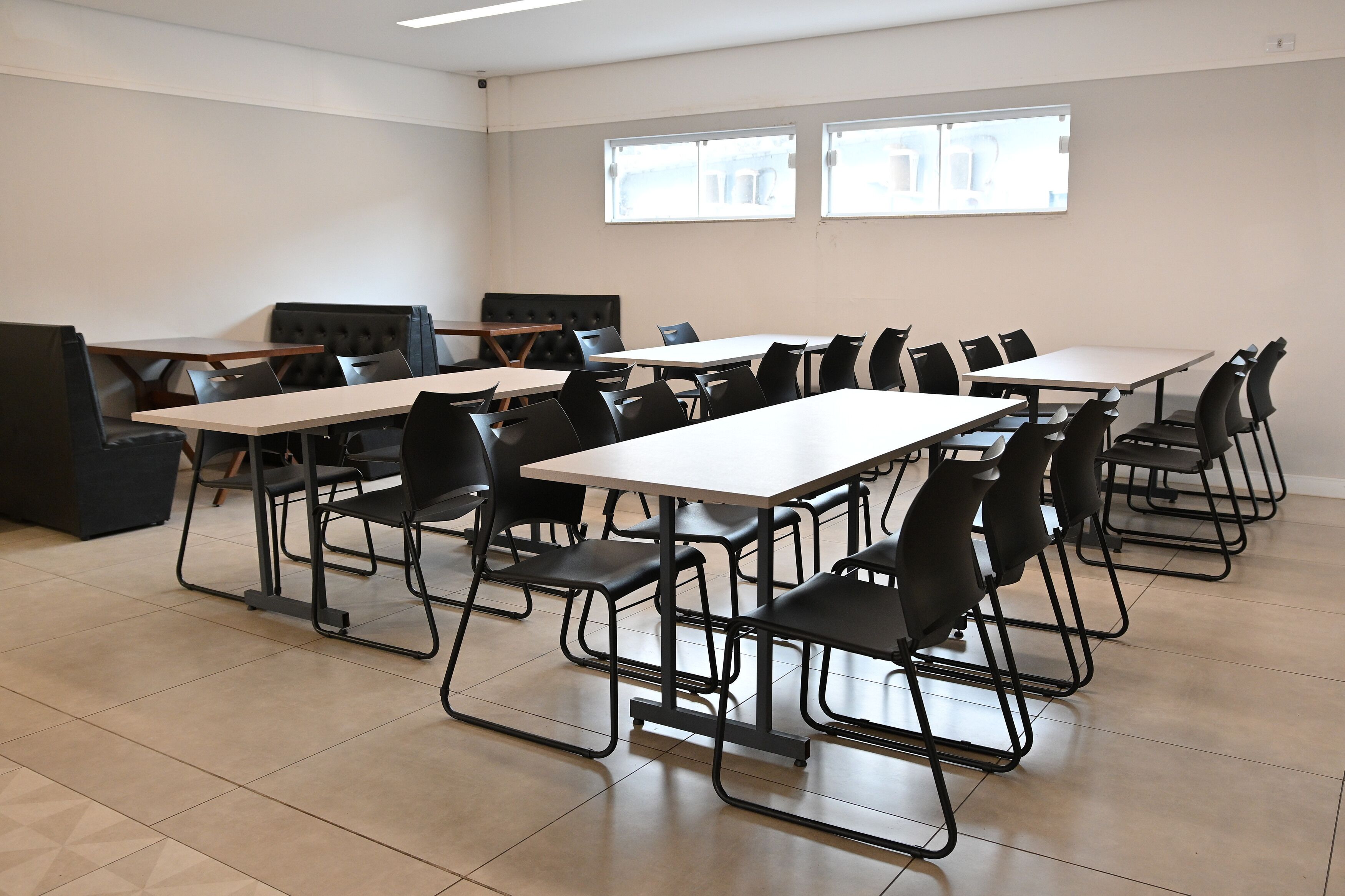 Uma sala de conferências com várias mesas e cadeiras, janelas amplas e teto alto.