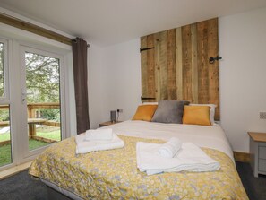 Quarto com cabeceira de madeira, cama com colcha floral amarela, duas almofadas e um conjunto de toalhas.