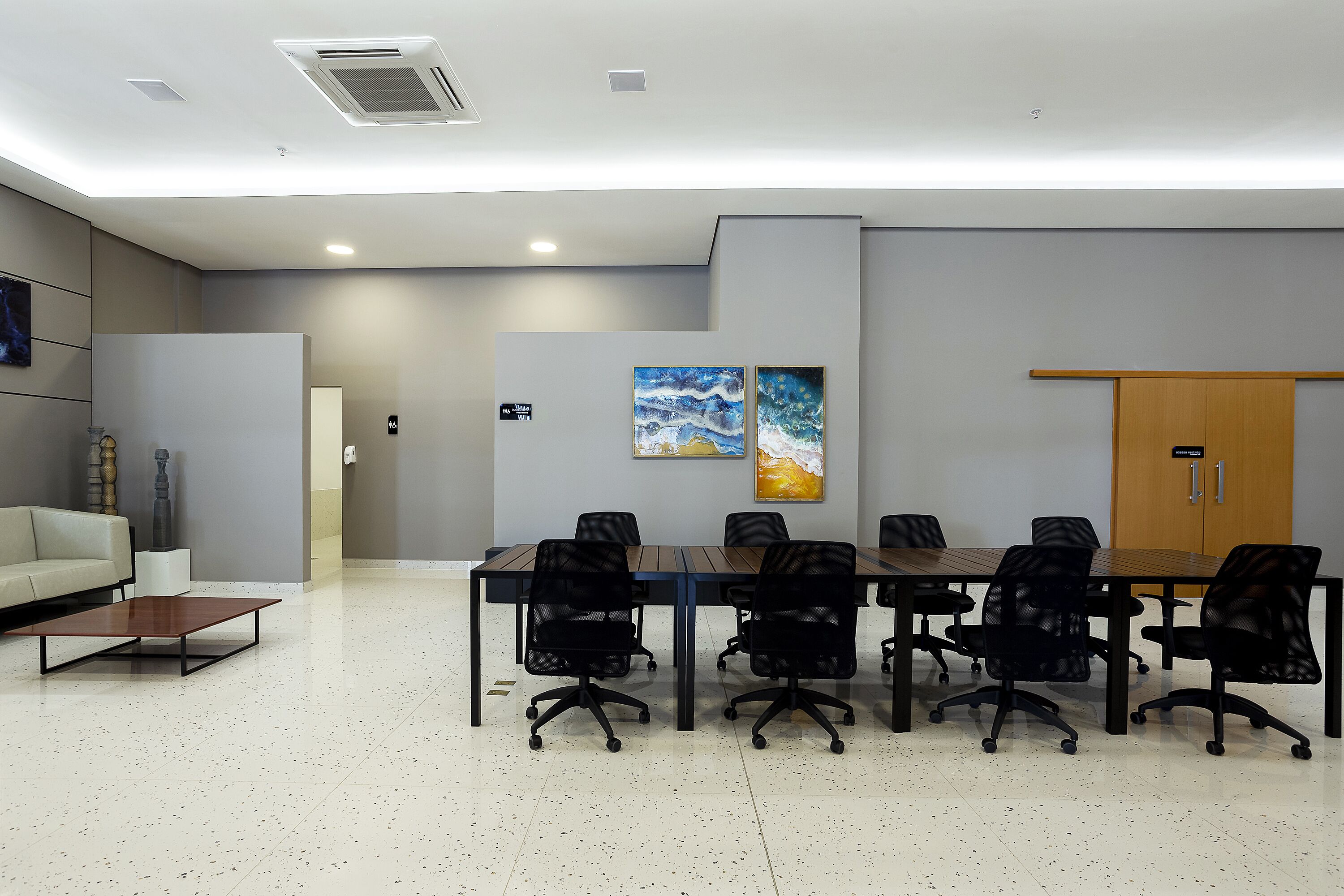 Uma sala de conferências com uma mesa comprida, seis cadeiras, um sofá e obras de arte nas paredes.