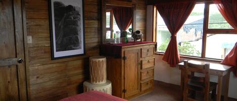 Um quarto de madeira com uma cama, cômoda, cadeira e janela com cortinas.
